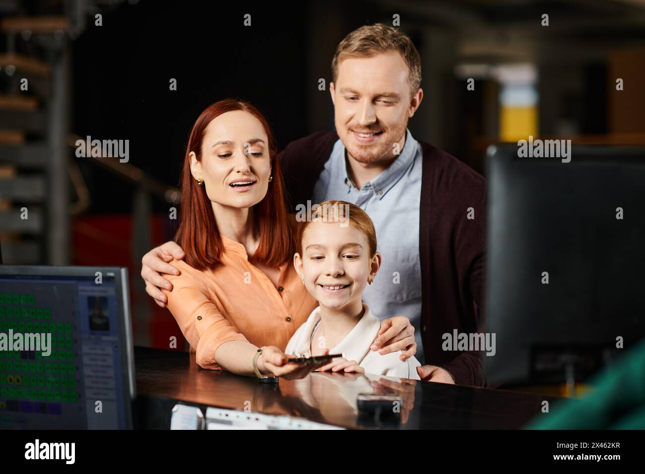 A man, woman, and child stand together, engrossed in a computer screen ...