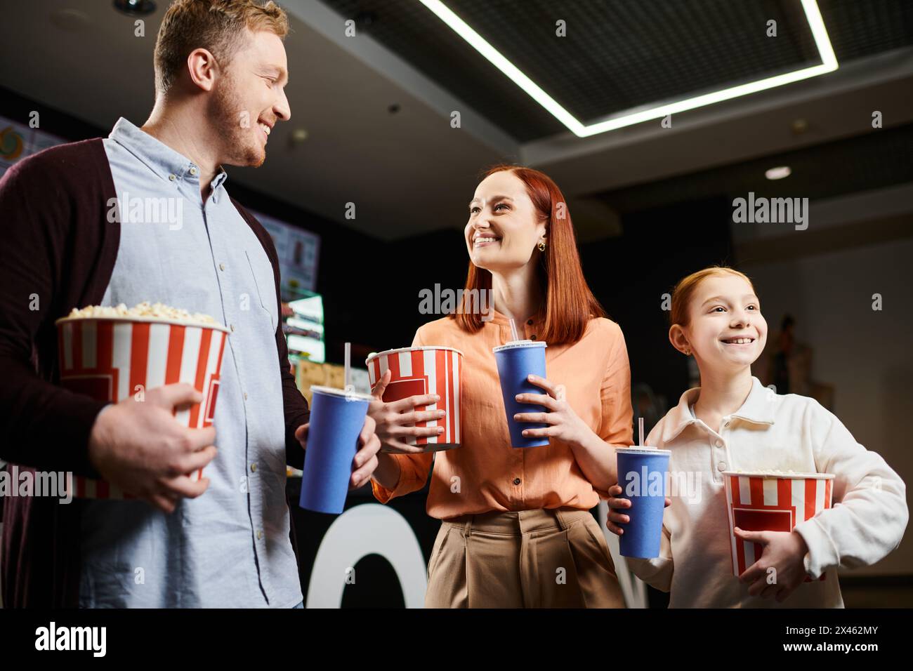 A happy family stands in a circle, holding popcorn while enjoying ...