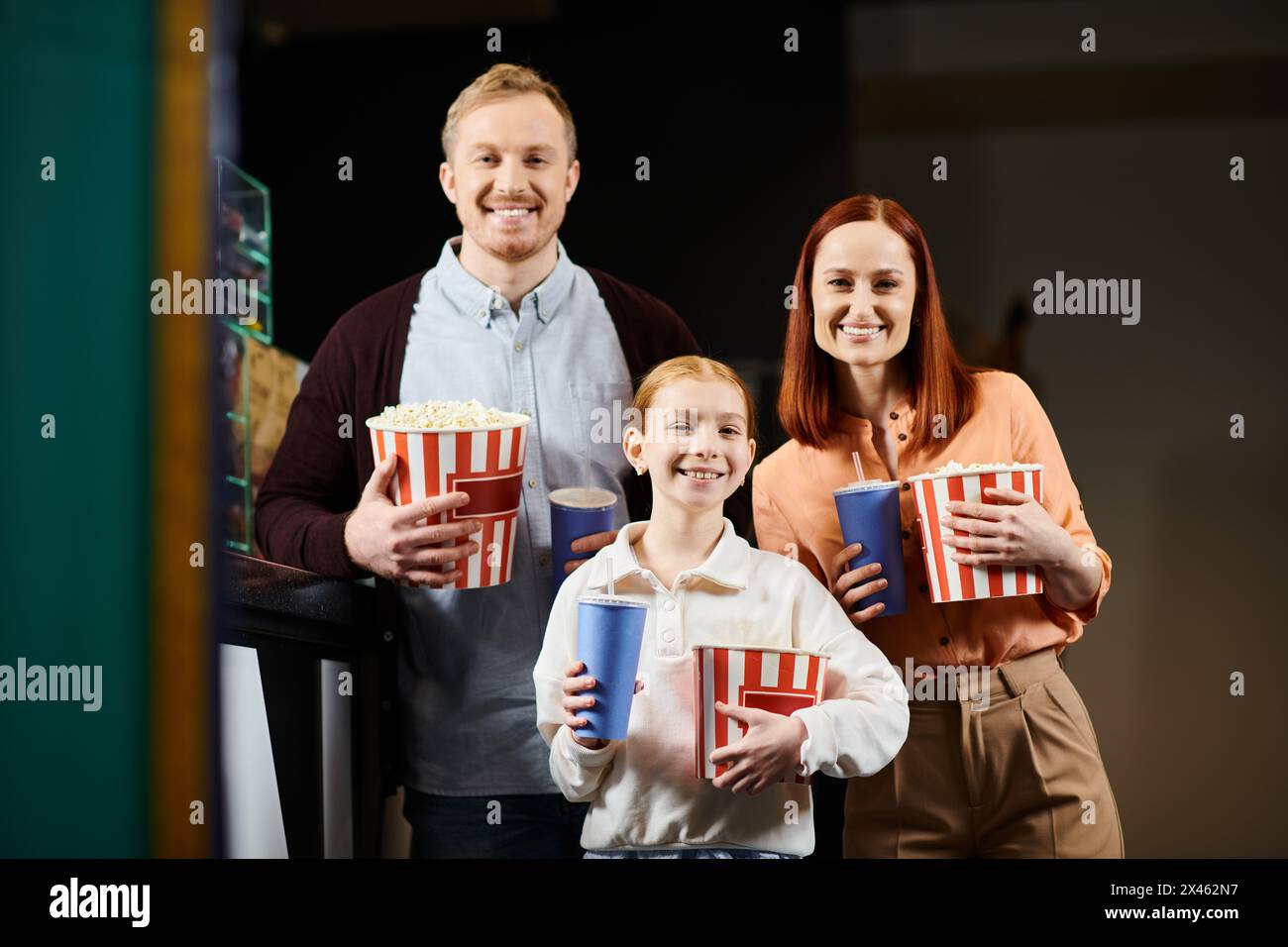 A man, woman, and child joyfully hold popcorn boxes at the cinema ...