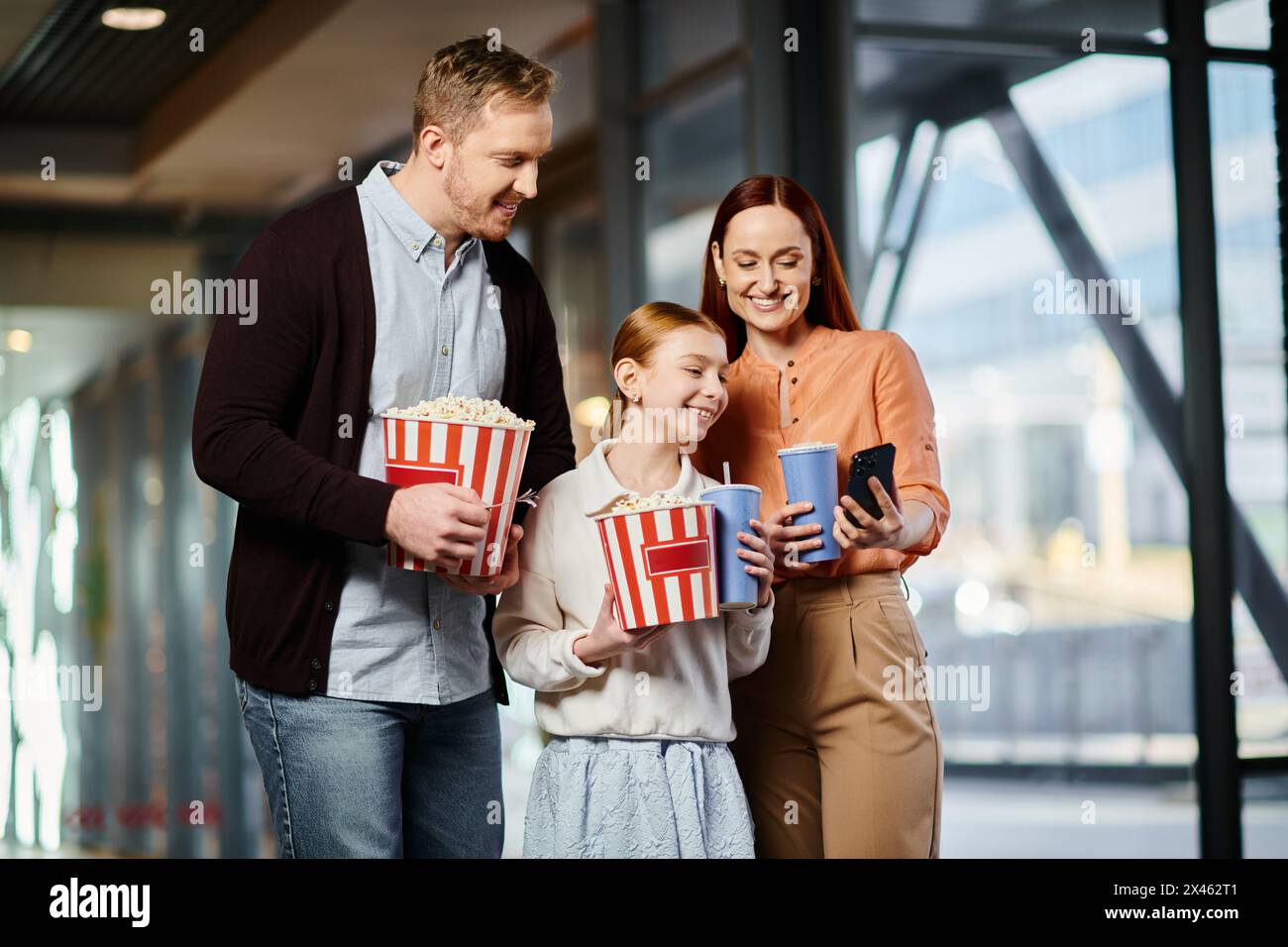 A man, woman, and child happily hold popcorn boxes while enjoying a ...