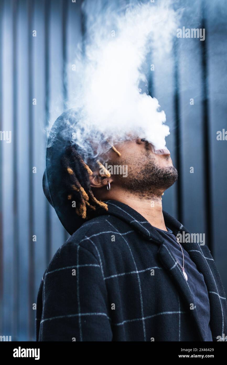 Side view of ethnic back guy with dreadlocks and hat in dense cloud of ...