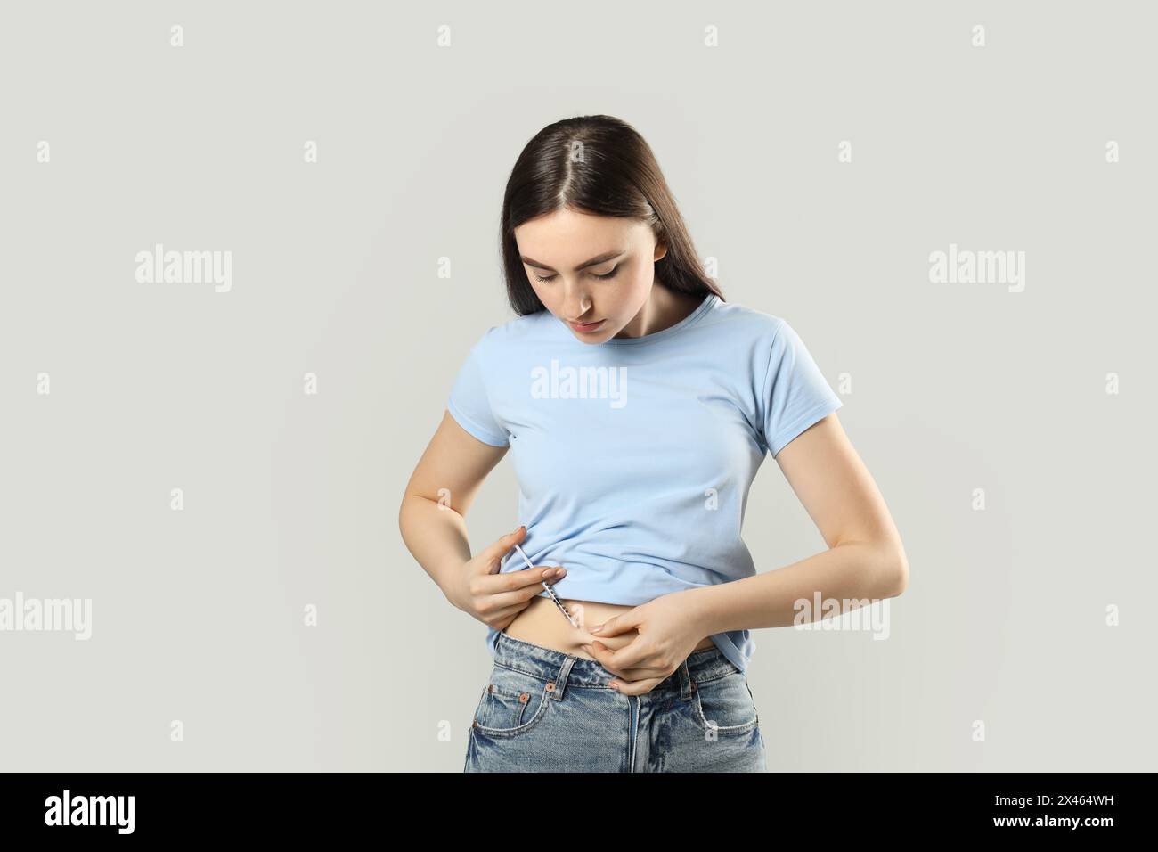 Diabetes. Woman making insulin injection into her belly on grey ...