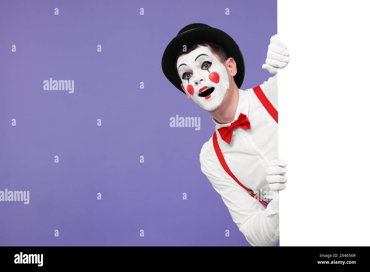 Funny mime artist peeking out of blank poster on purple background ...
