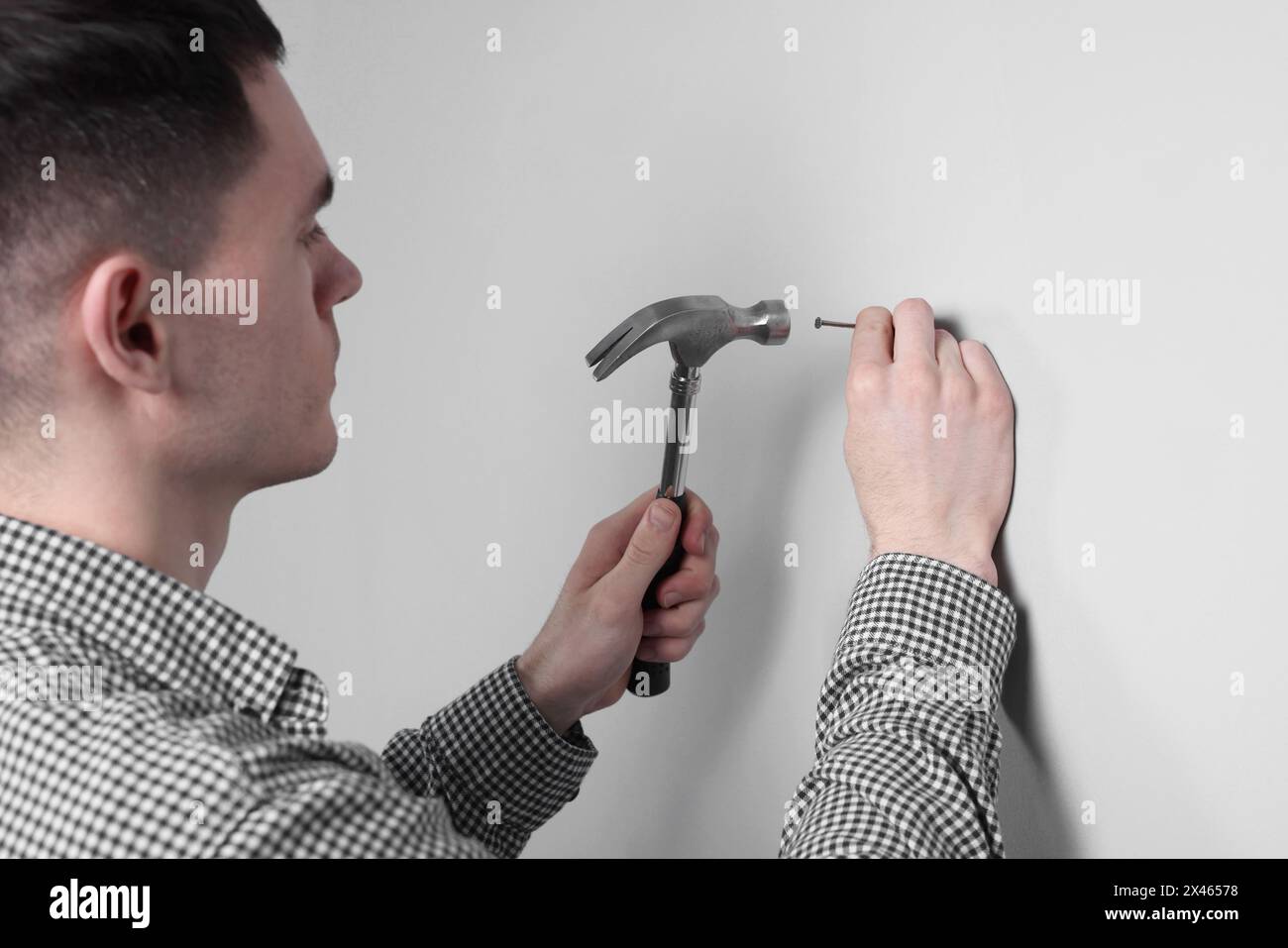 Young man hammering nail into white wall indoors Stock Photo - Alamy