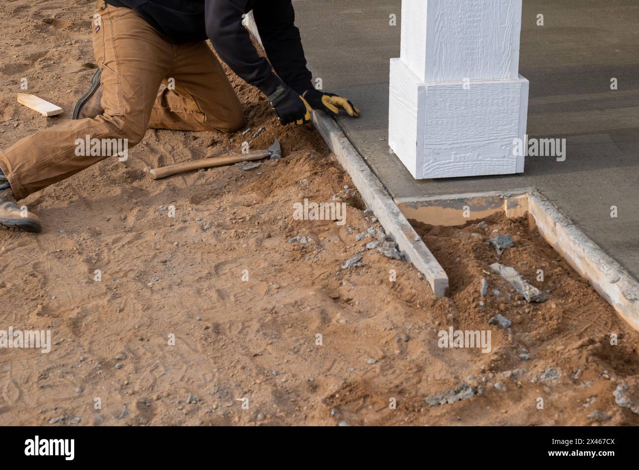 Worker removing wood form from edge of new concrete cement sidewalk, at ...