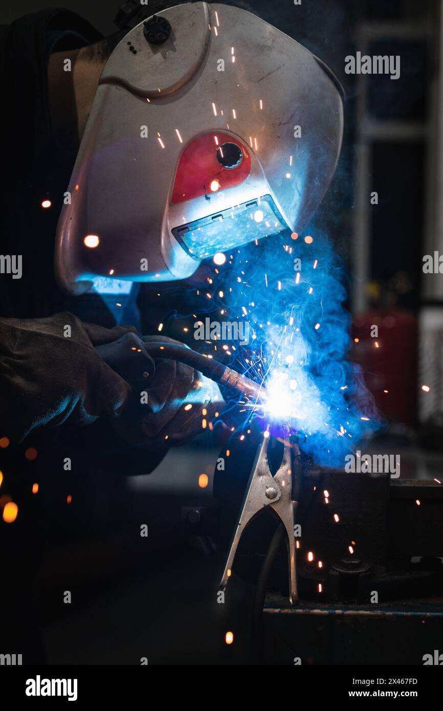 Side view of unrecognizable repairman in protective helmet using torch ...