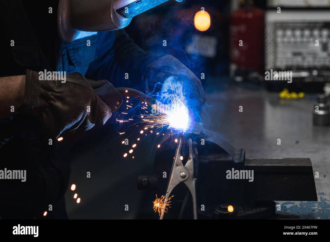 Side view of unrecognizable repairman in protective helmet using torch ...