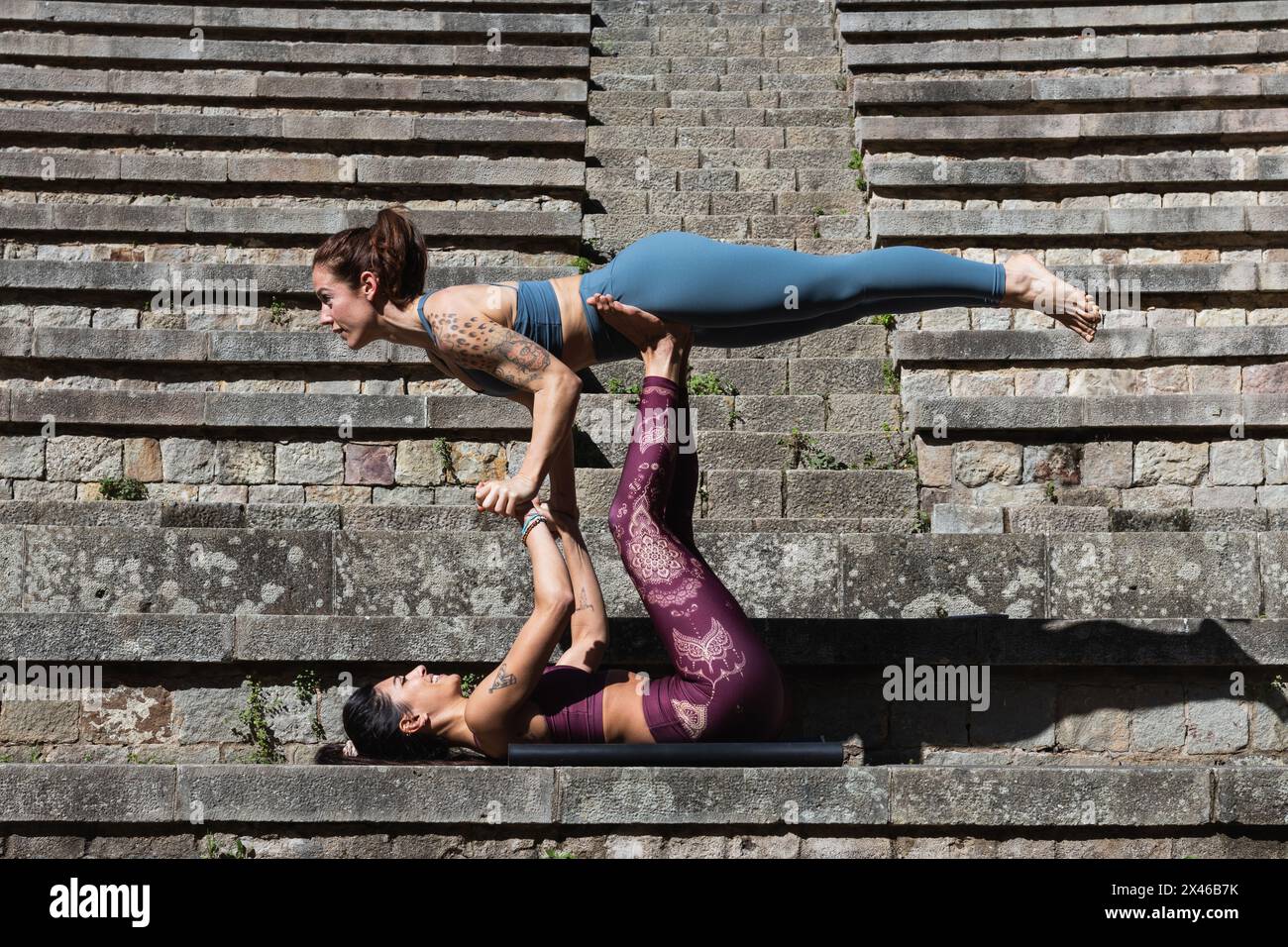 Side view of flexible female supporting woman on legs while practicing ...