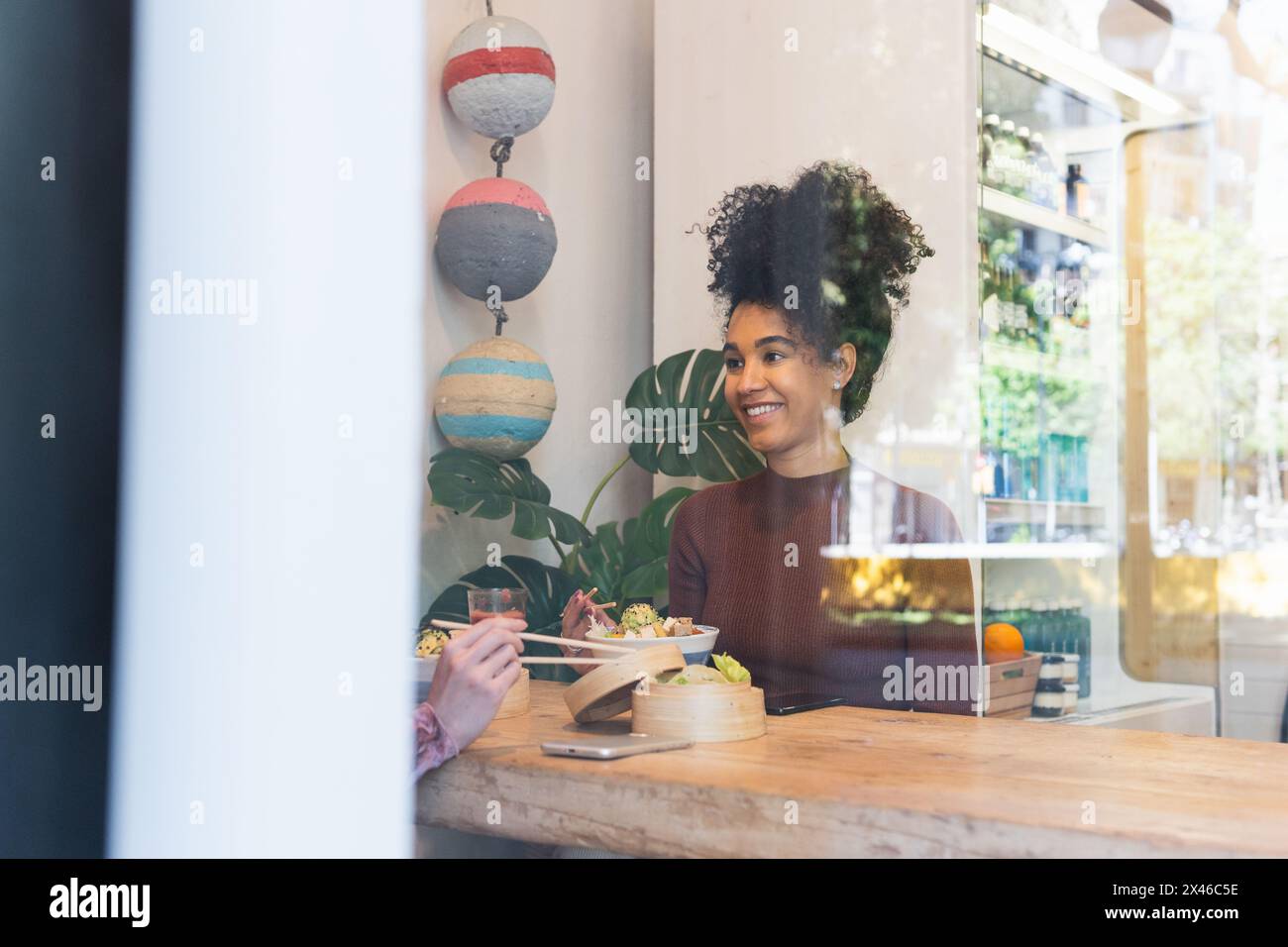Smiling black woman eating poke while sitting at table with crop ...