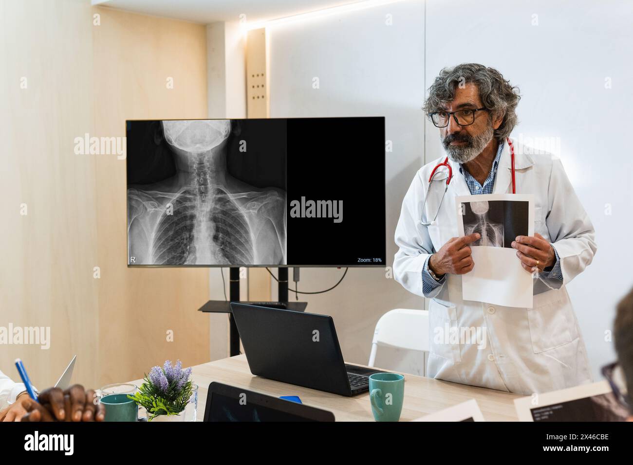 Elderly male medic explaining x ray image to unrecognizable coworkers ...