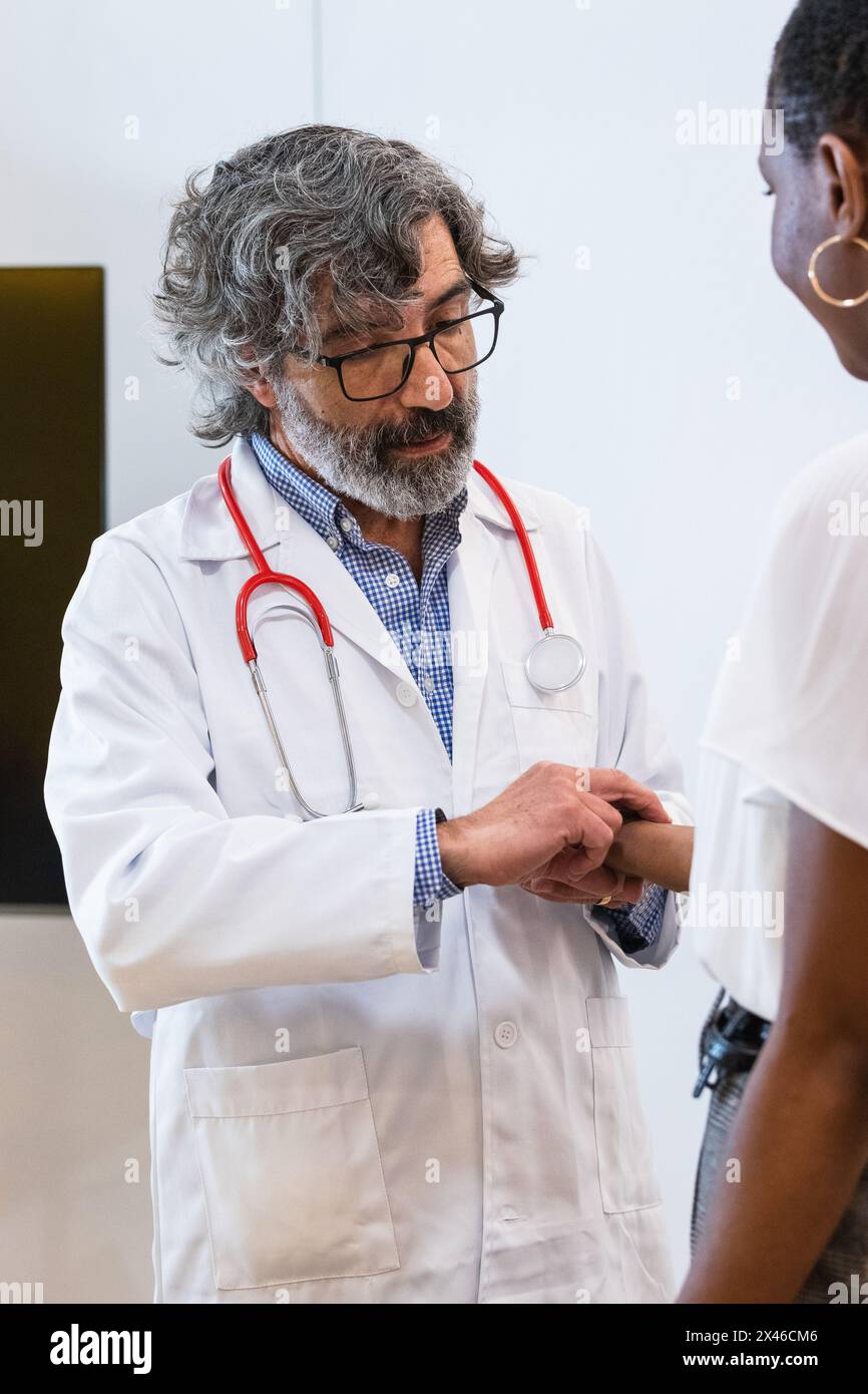 Focused senior male doctor measuring pulse of black female patient ...