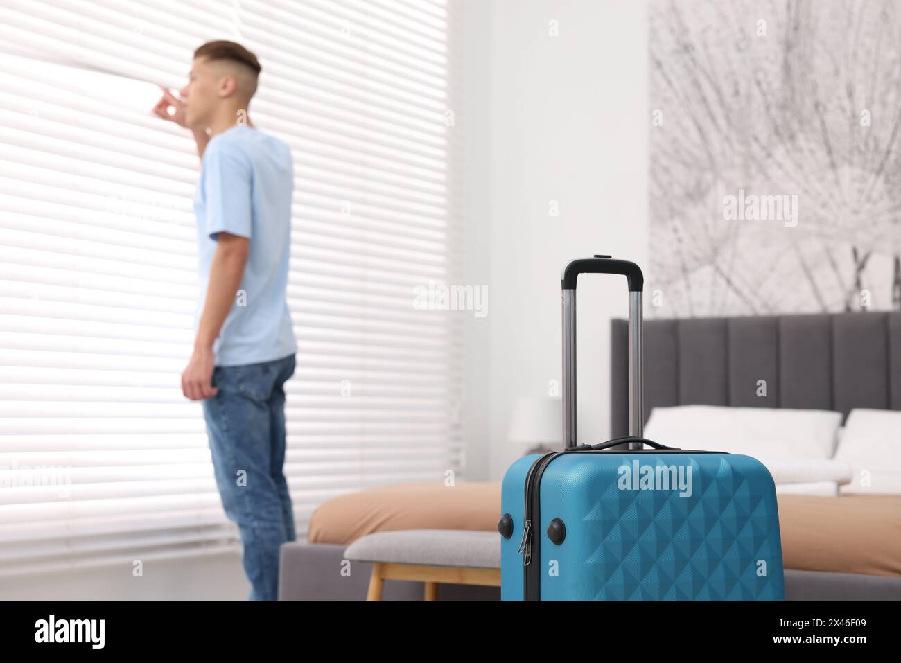 Guest looking through blinds in stylish hotel room, focus on suitcase ...