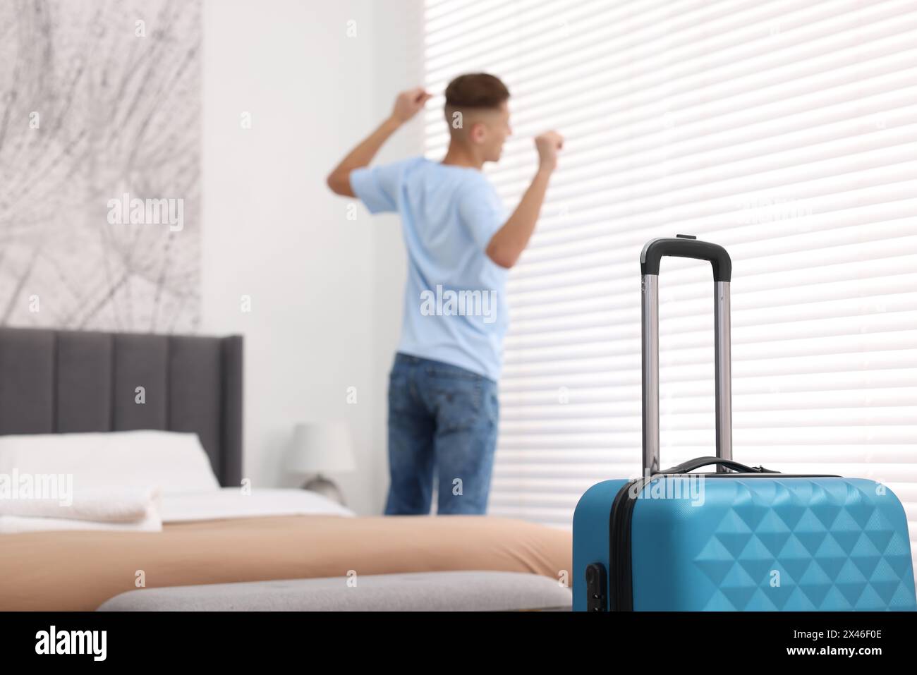 Guest stretching in stylish hotel room, focus on suitcase Stock Photo ...