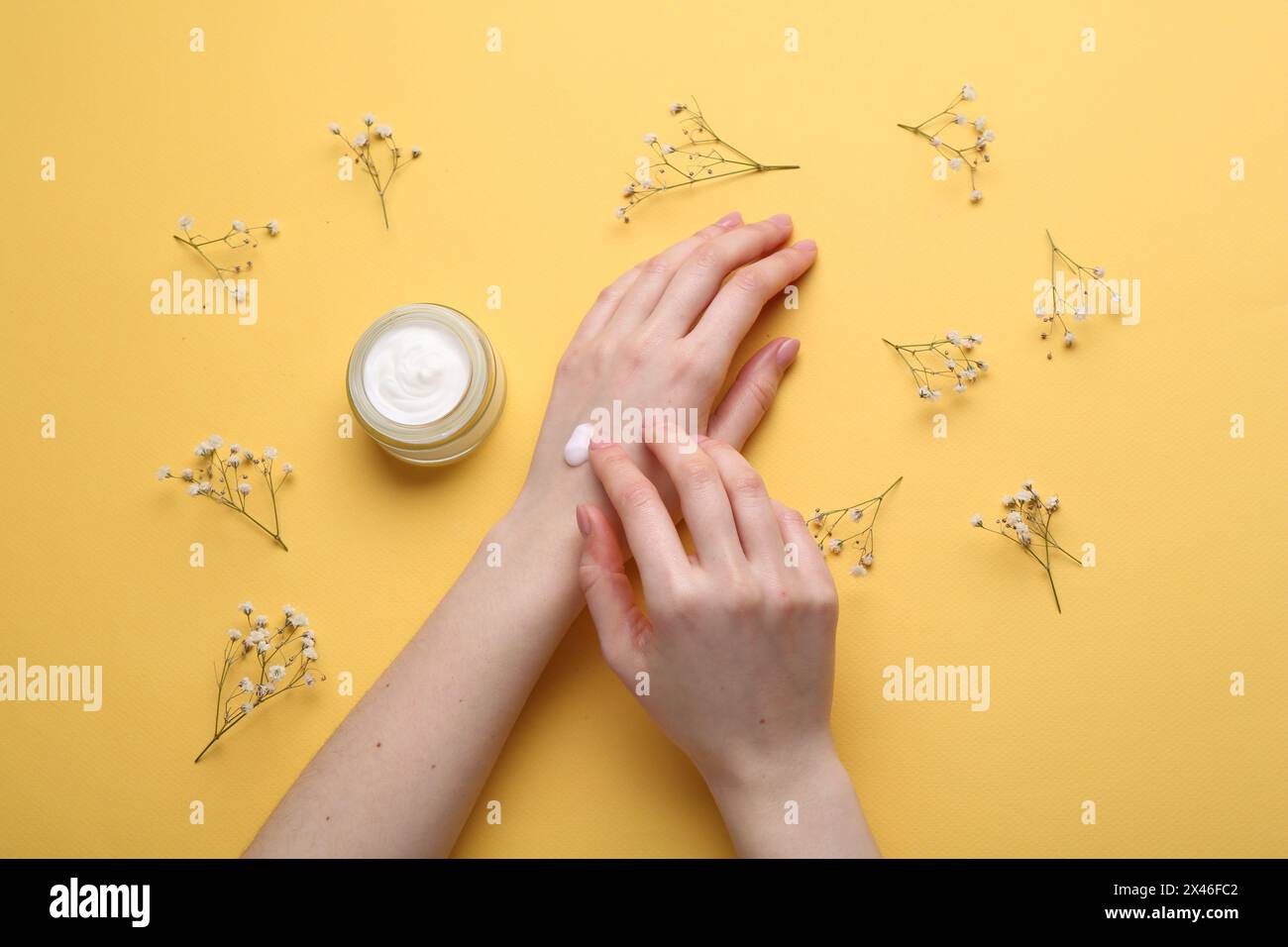 Woman applying hand cream and flowers on yellow background, top view ...