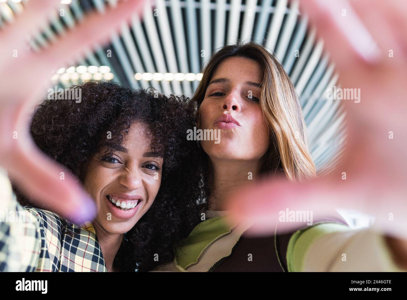 Cheerful ethnic woman near best friend with pouting lips showing focus ...