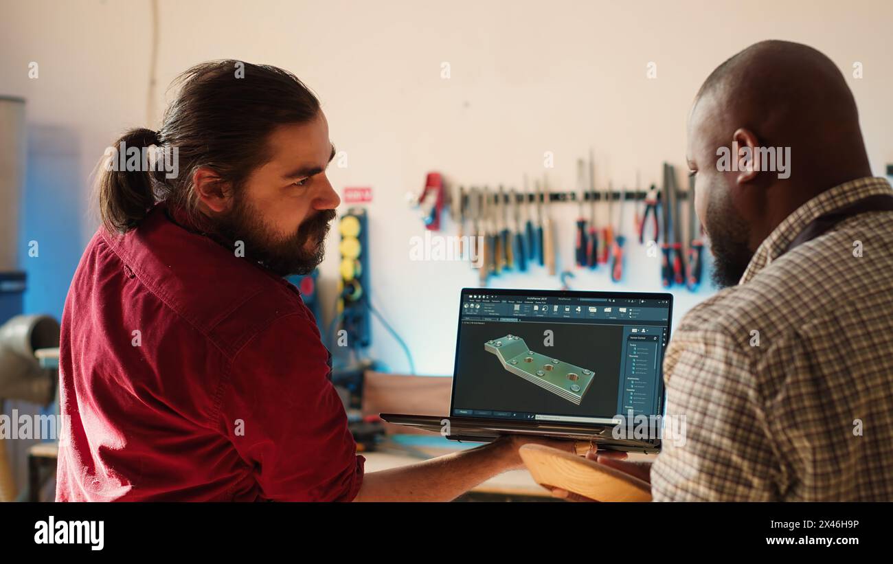 Woodworker looking over blueprints on laptop in CAD software with apprentice. Manufacturer and ...