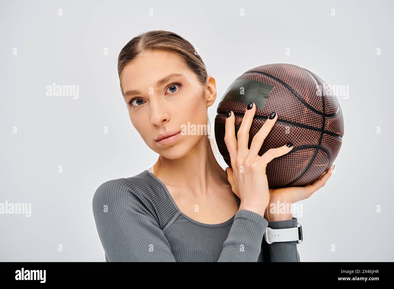 A sporty young woman in active wear holding a basketball over her face ...