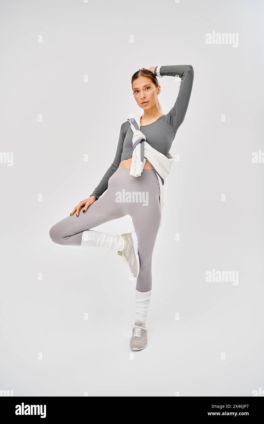A sporty young woman in grey and white activewear gracefully performs a ...