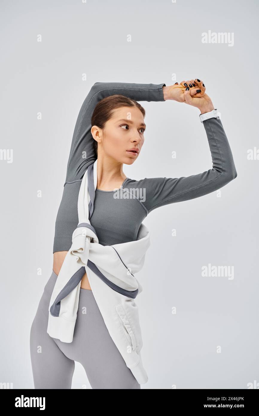 A sporty young woman in grey and white attire striking a pose against a ...