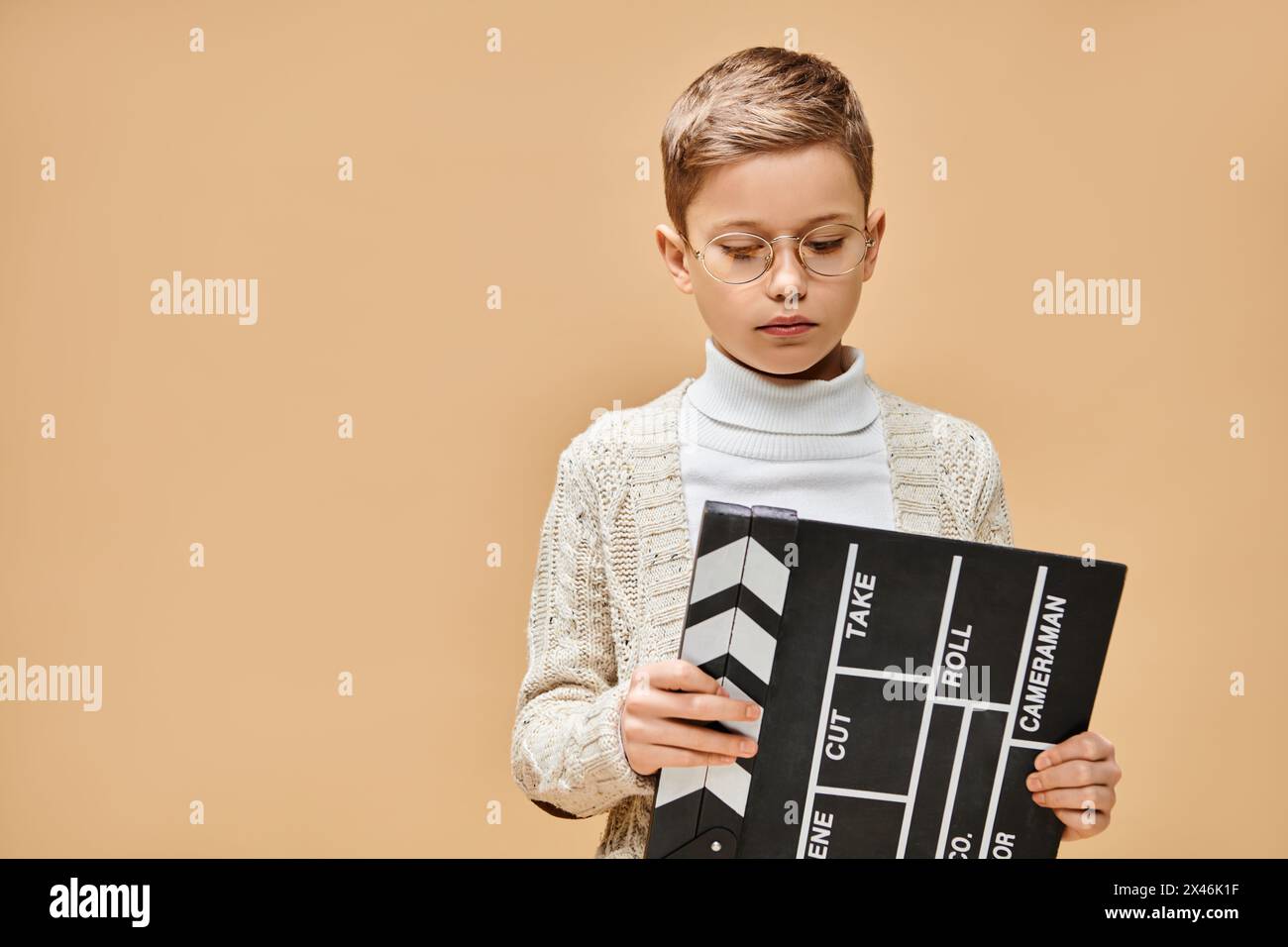 A cute preadolescent boy dressed as a film director holding a black and ...