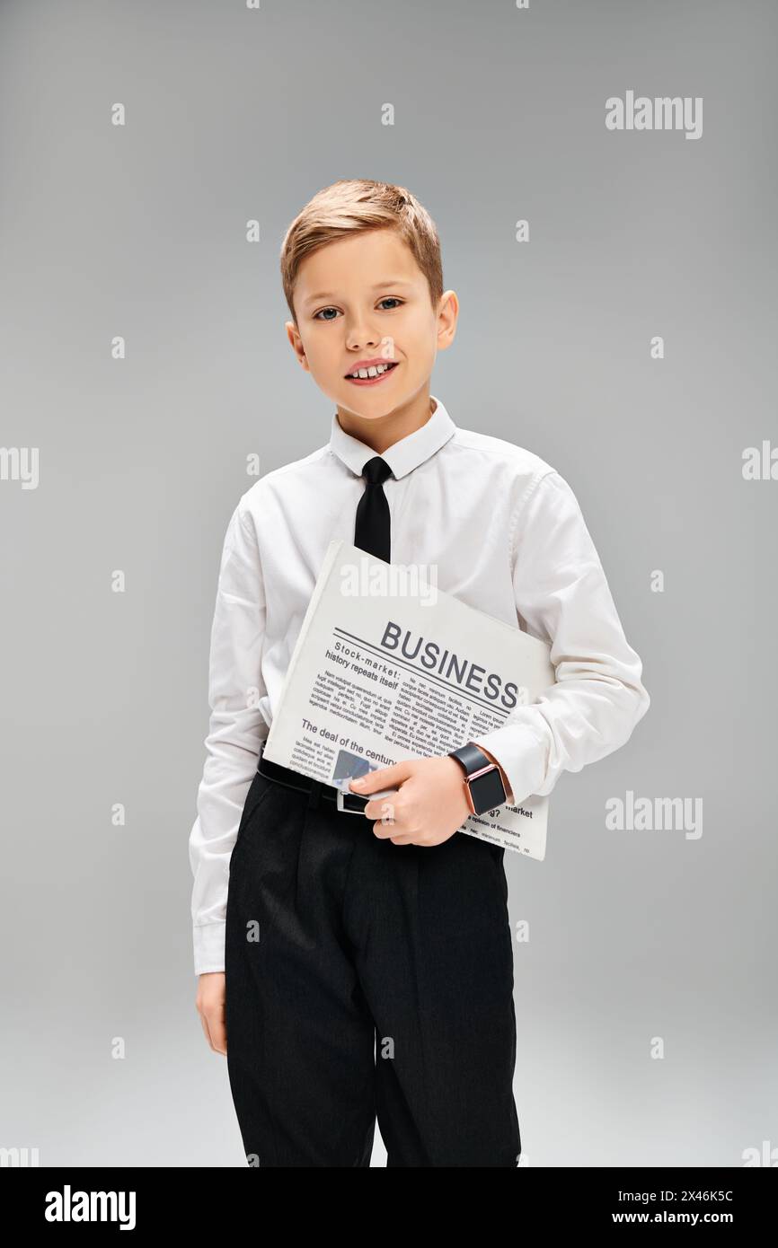 Young boy in formal attire holding a newspaper against a gray backdrop ...