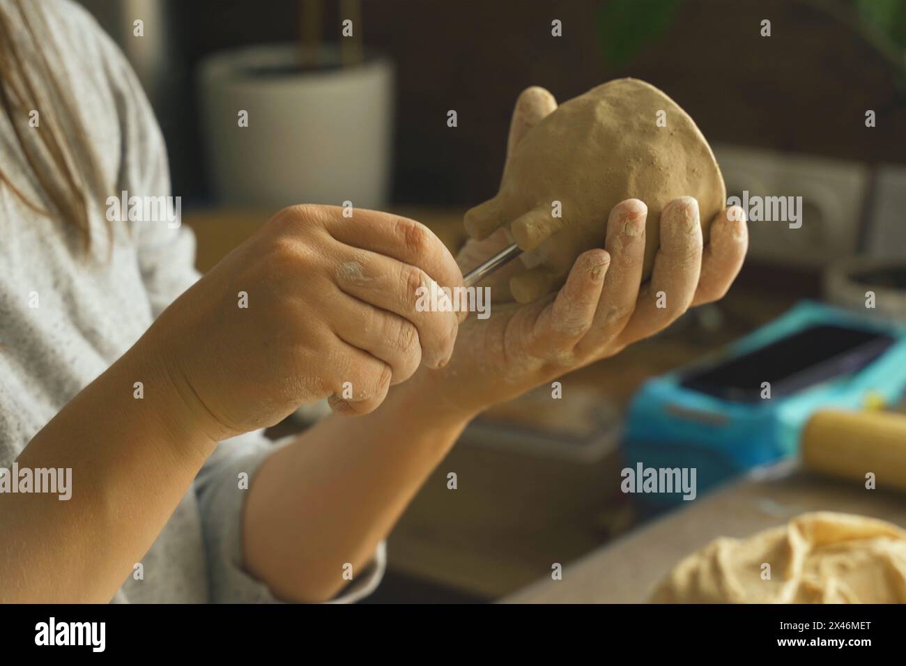 A woman makes holes using a tool in a clay craft - a candlestick. Close ...