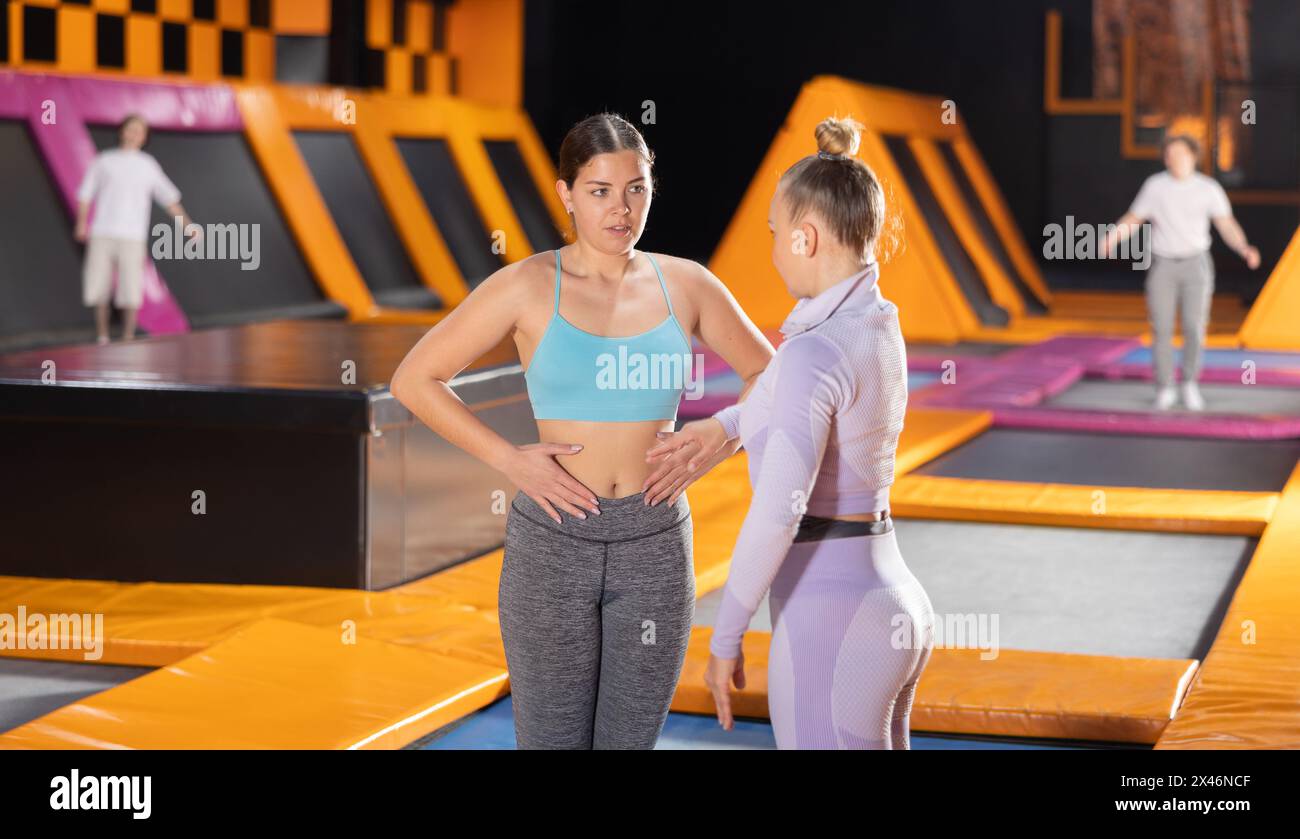 Portrait of female trampolining coach showing young woman jumping ...