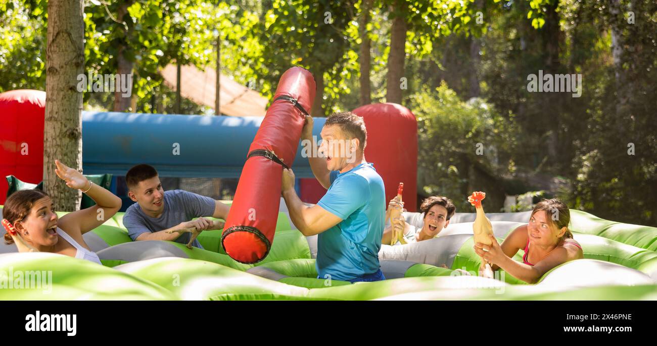 Playful man fighting off friends with inflatable log while guarding toy ...