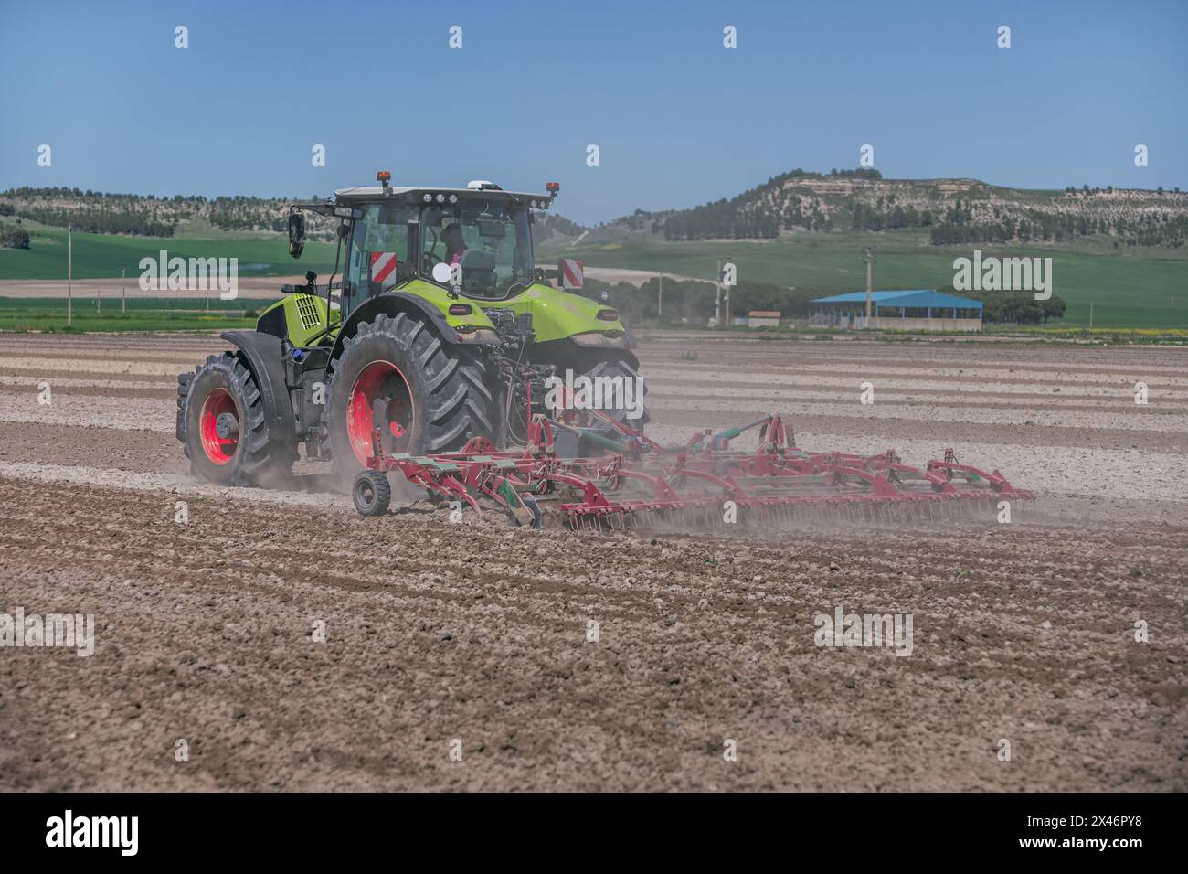 A green tractor pulling a plow through a crop field Stock Photo - Alamy