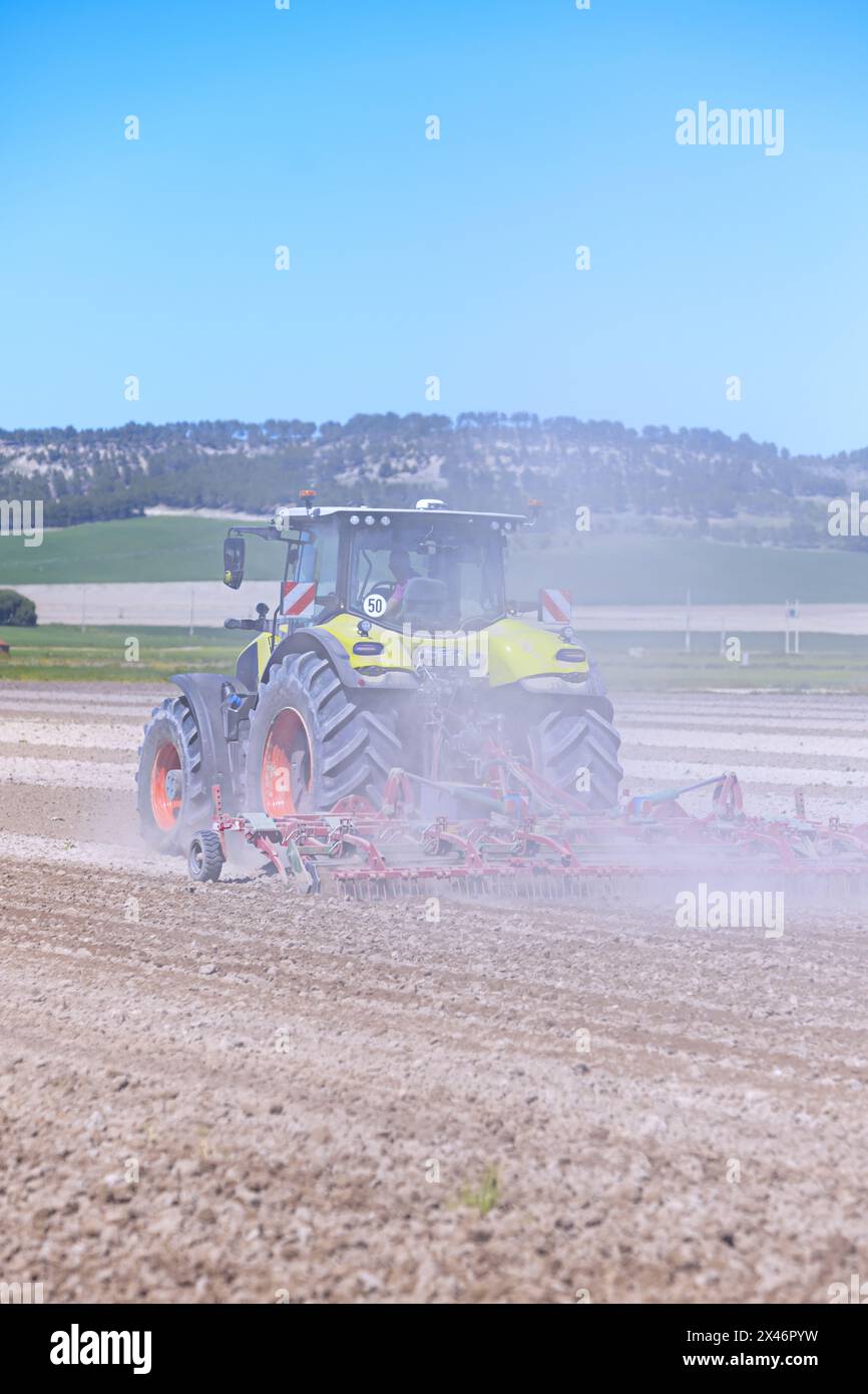 A green tractor pulling a red plow across a dusty crop field with a ...