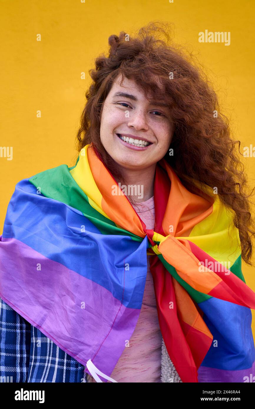 Portrait of cheerful non-binary person red hair with rainbow flag over ...