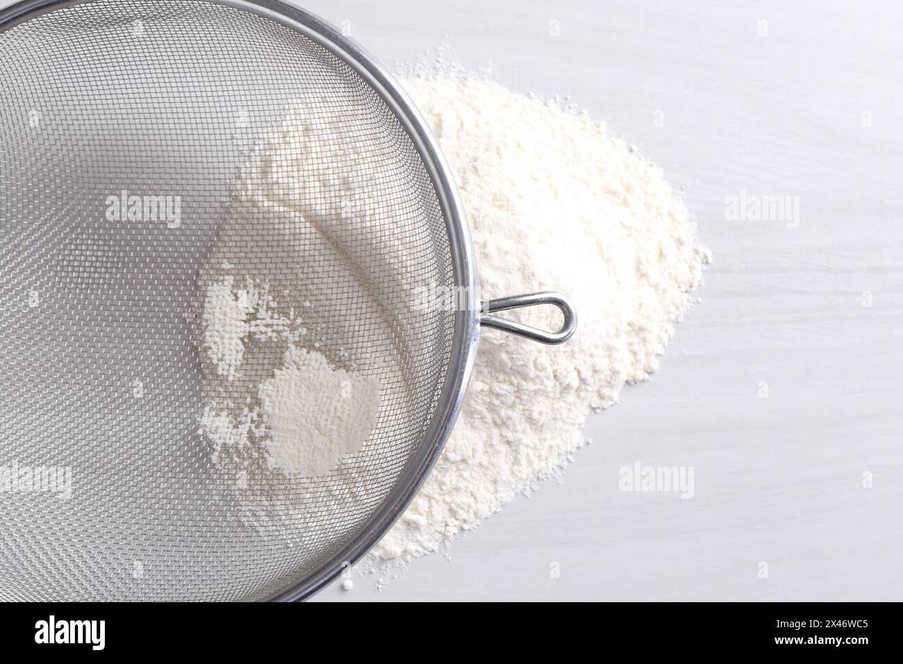 Metal sieve and flour on white wooden table, top view. Space for text ...