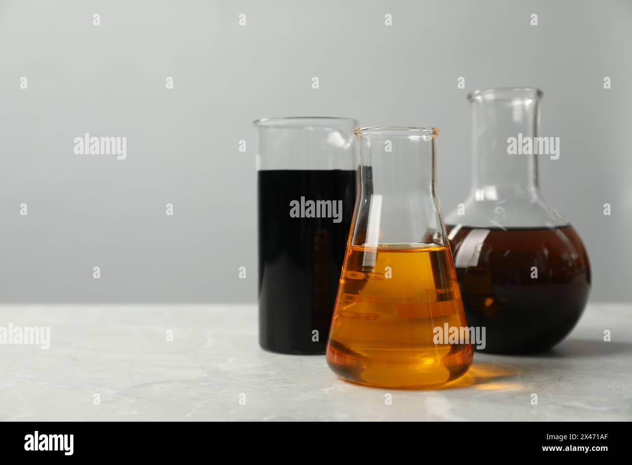 Beaker and flasks with different types of oil on white table, space for ...