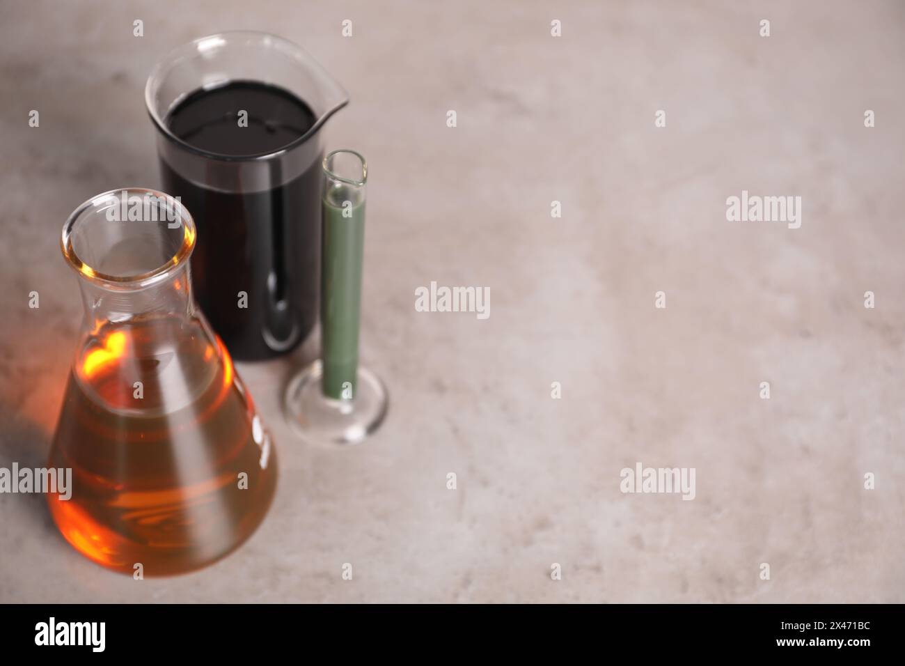 Test tube, beaker and flask with different types of oil on grey table ...