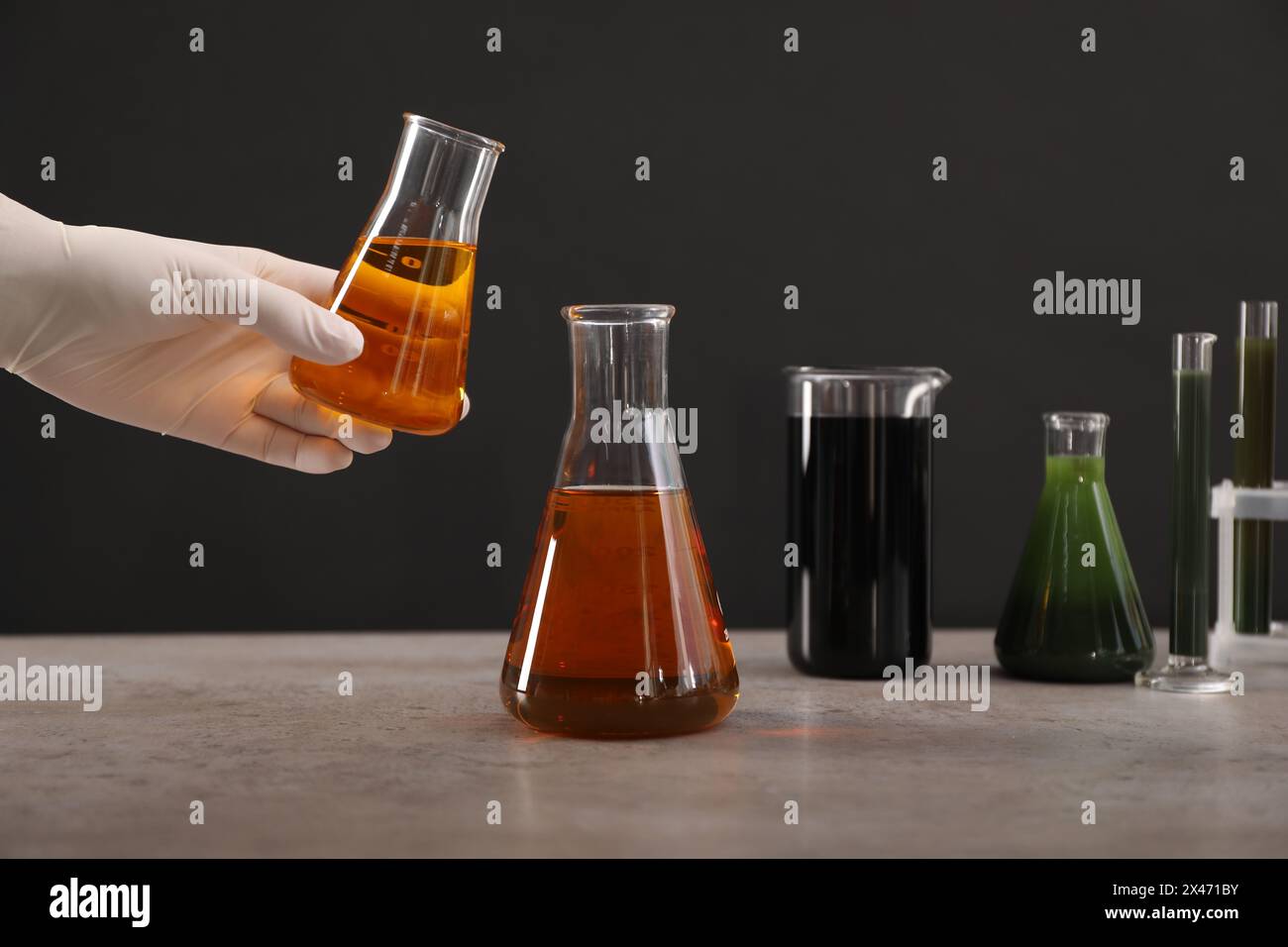 Woman holding flask with yellow crude oil over grey table against dark ...