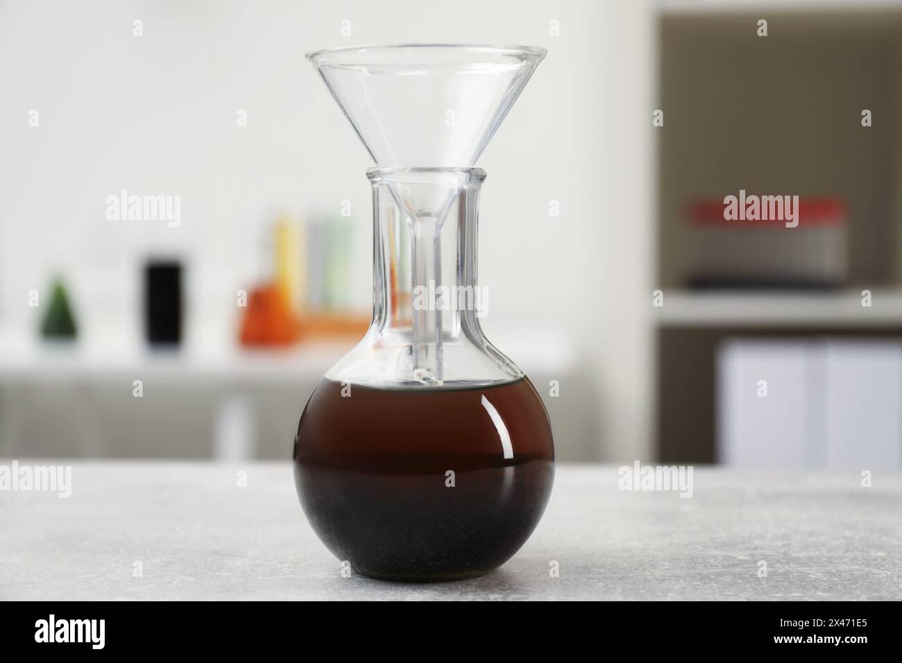 Flask with brown crude oil and filter funnel on light grey table Stock ...