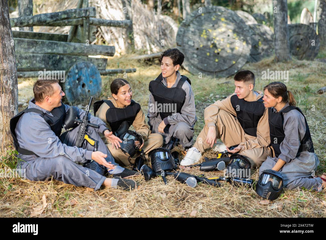 Group of male and female paintball players sitting on ground and ...