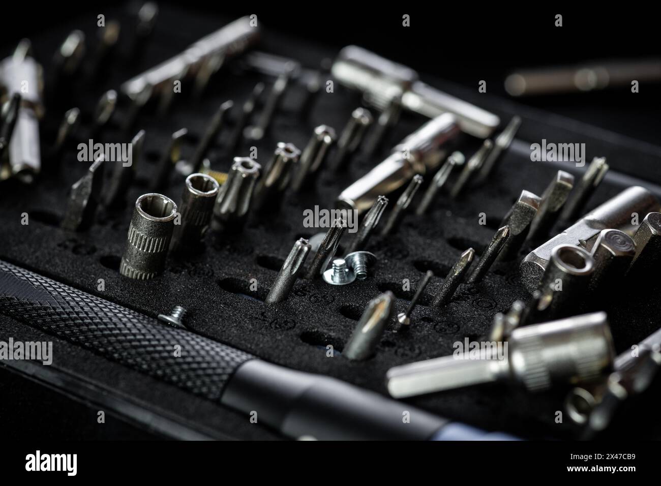 Unorganized screwdriver kit with aluminum bit driver on black tray ...