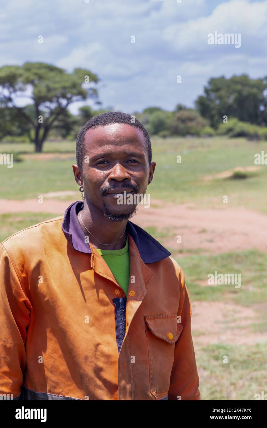 village young african worker ,wearing orange workwear ,green field and ...