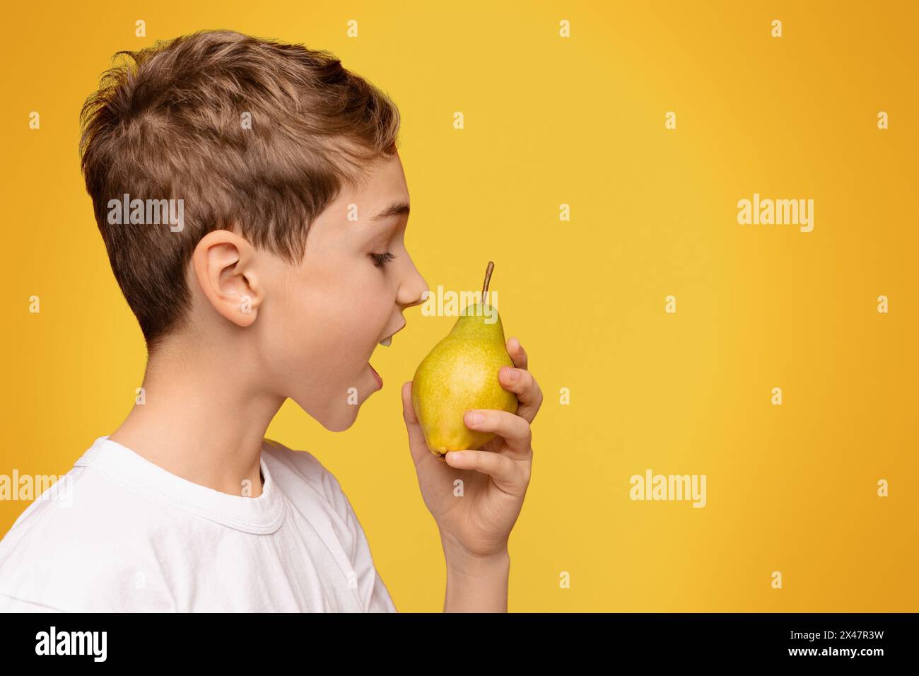 Teen boy biting fresh pear, side view Stock Photo - Alamy