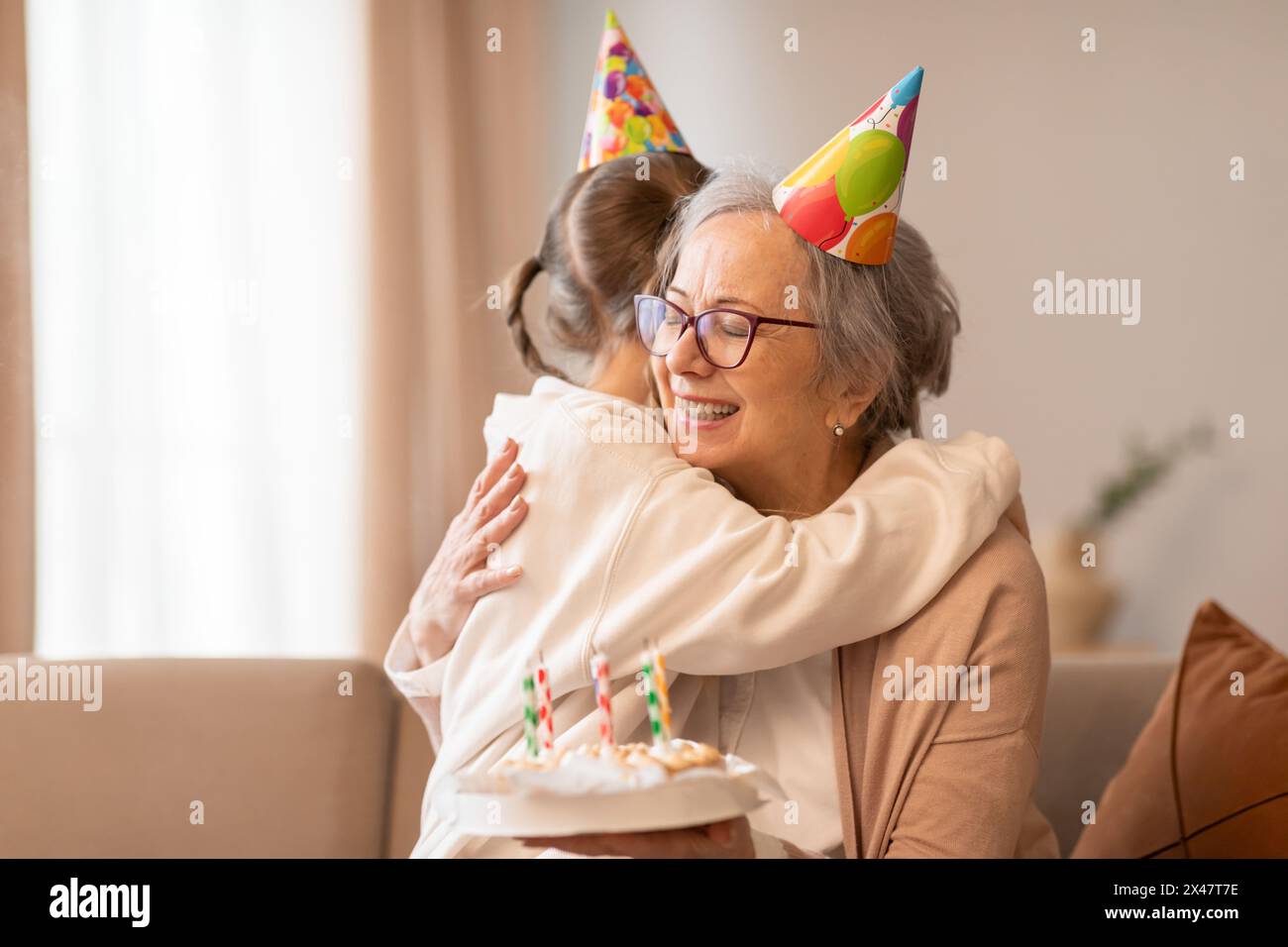 Older Woman Hugging Young Girl With Birthday Hats On Stock Photo - Alamy