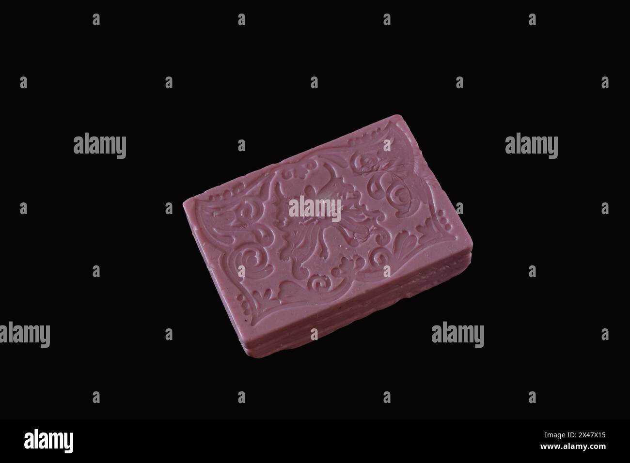 On a black background lies a square-shaped purple soap made at home ...