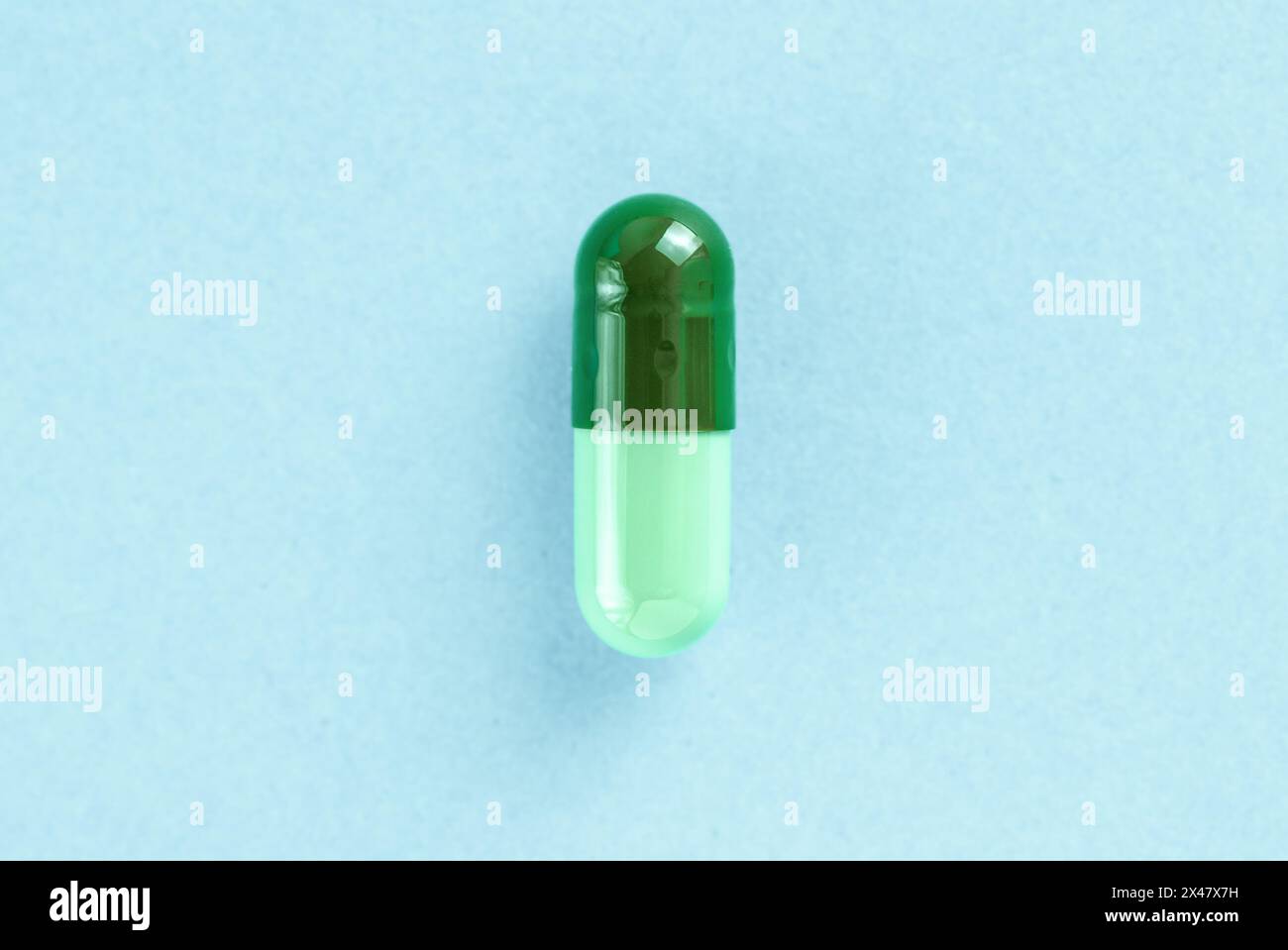 Green two-piece hard starch capsule on blue background with copy space ...