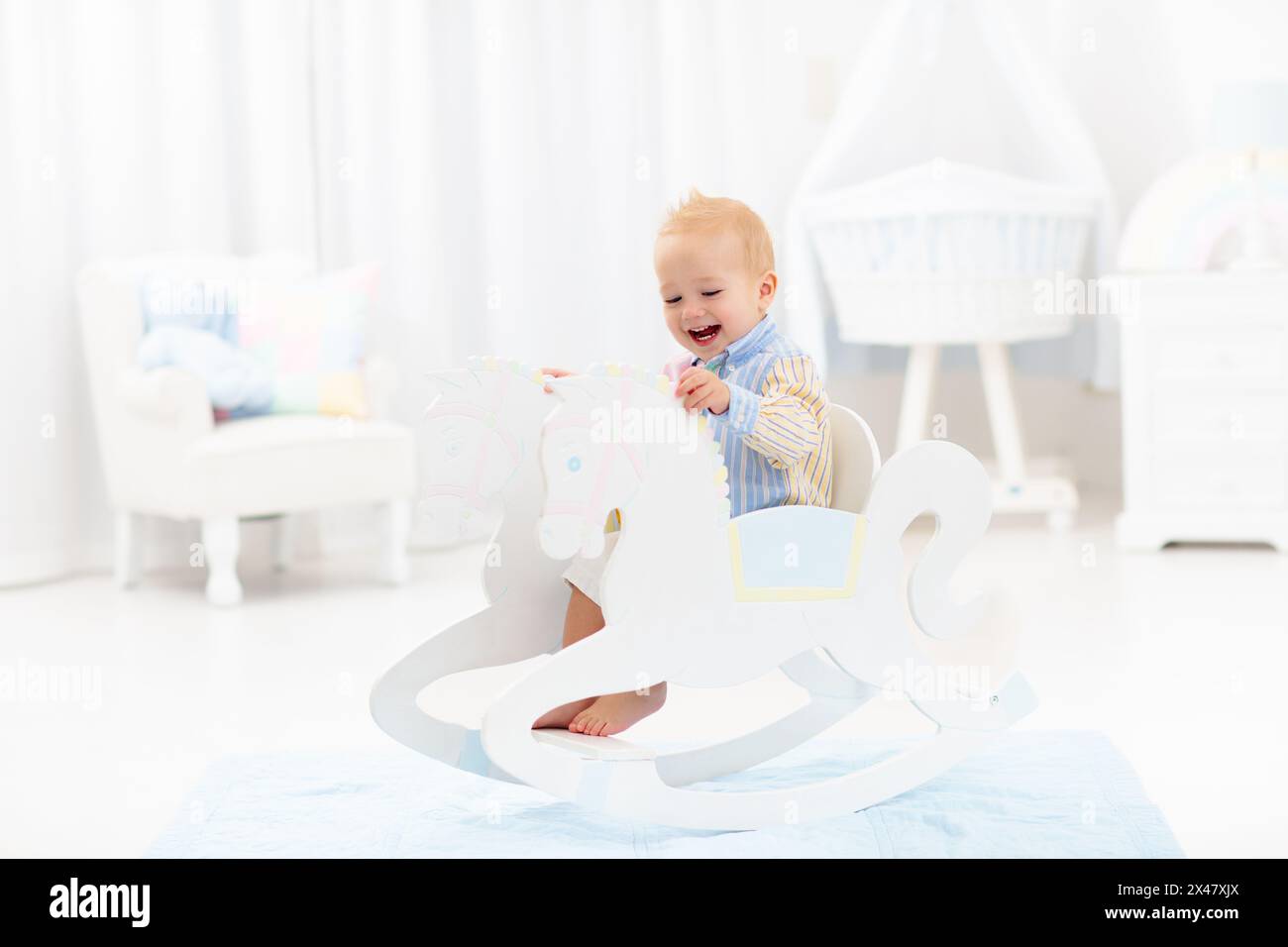 Cute baby boy riding wooden traditional rocking horse toy in white ...