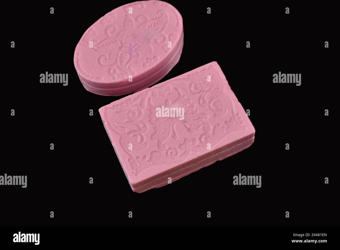 On a black background lie two pieces of oval and square pink soap, made ...