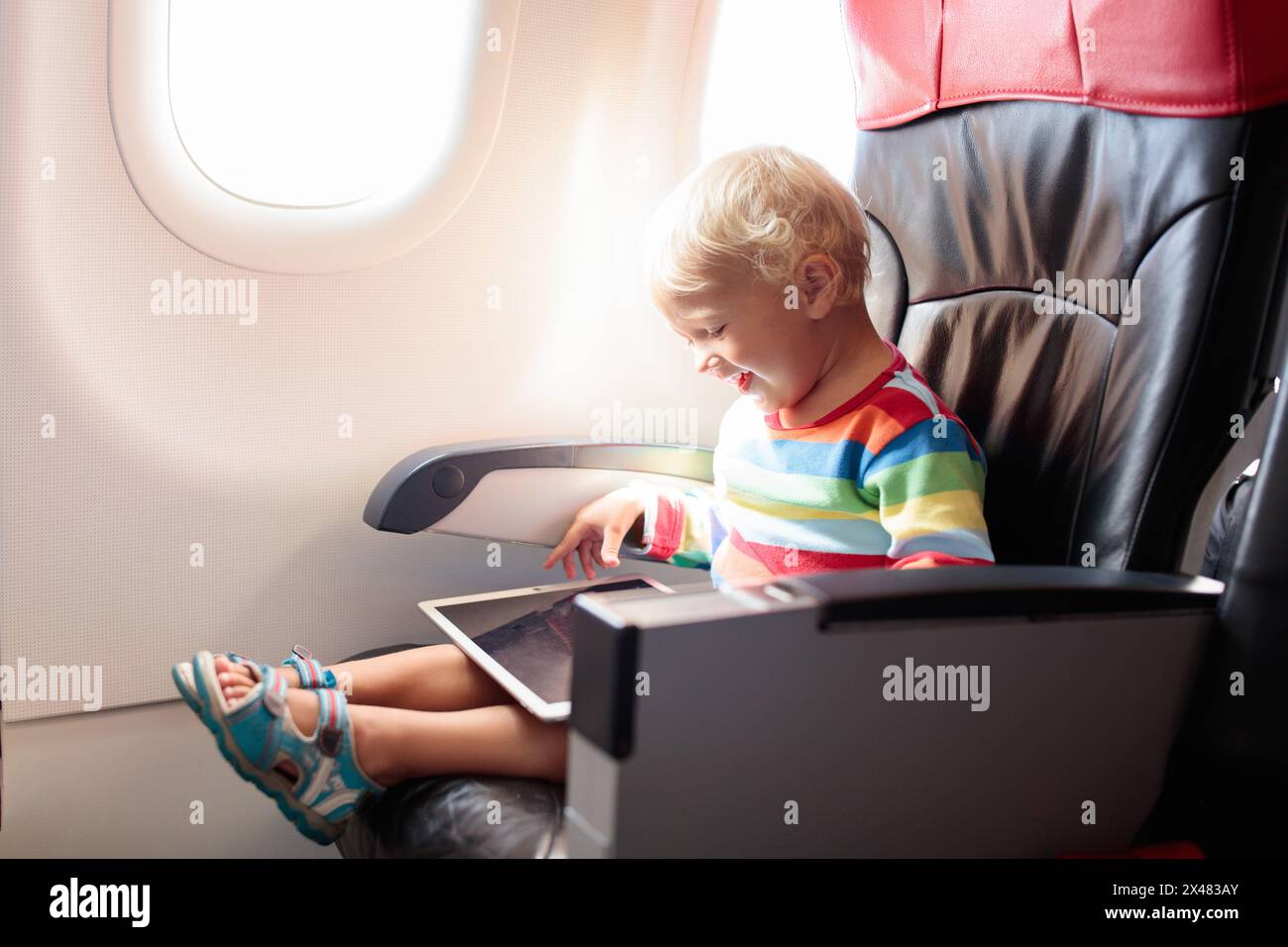 Child in airplane. Kid in air plane sitting in window seat playing game ...