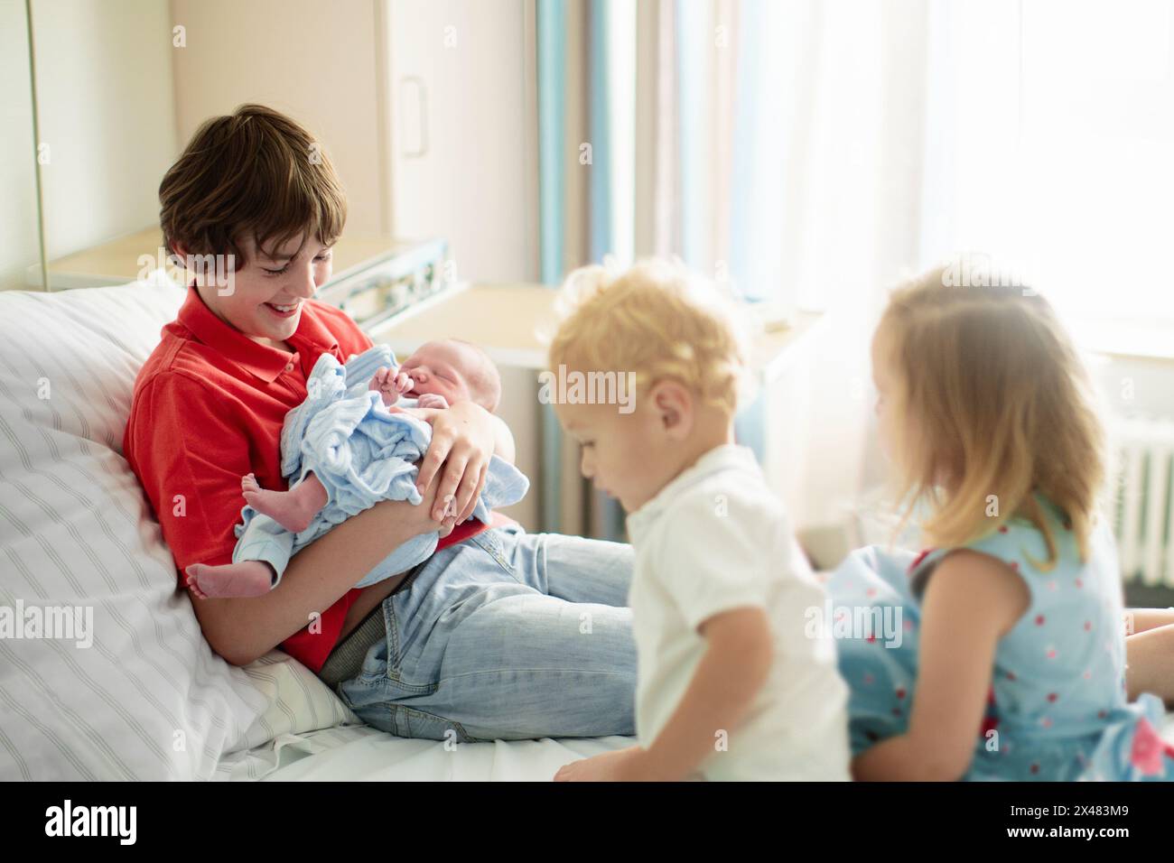Siblings meet newborn baby in hospital. Child holding new infant ...