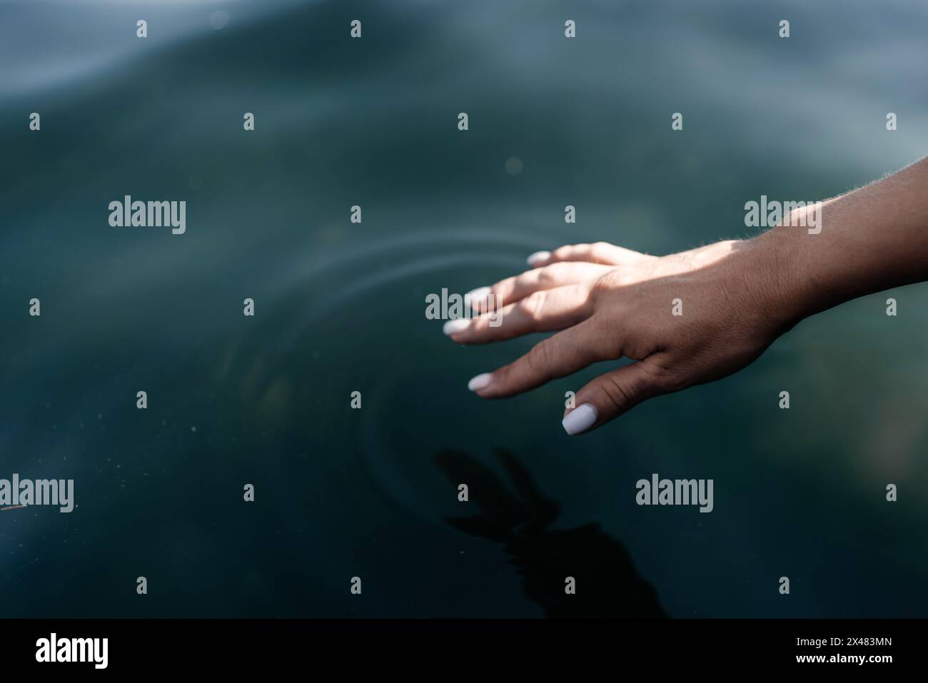 The hand touches the water, creating ripples. The water is calm and ...