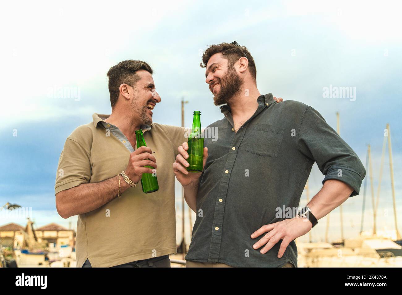 Two men - laughing and holding beers at marina - casual atmosphere ...