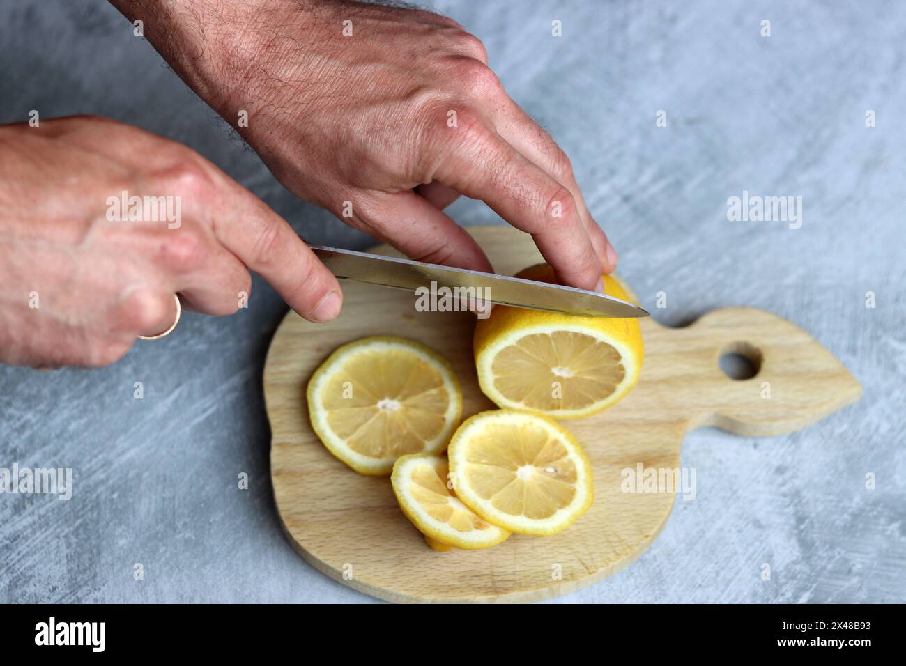 Male hands cutting lemon on wooden board. Grey background with copy ...